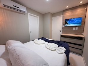 Quarto de hotel com uma cama, televisão fixada na parede e um aparelho de ar condicionado sobre a cama.