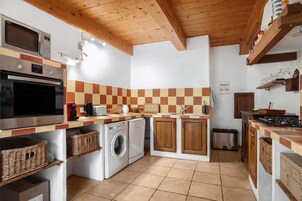 Cozinha compacta com micro-ondas, forno e máquina de lavar, armários de madeira e painel de azulejos.