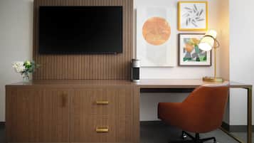 Quarto de hotel moderno com TV de tela plana fixada numa parede de painel de madeira, uma escrivaninha com cadeira e uma cafeteira.