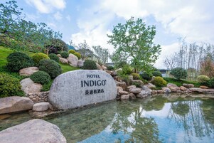 Placa de pedra do Hotel Indigo, com um lago e jardim ajardinado em primeiro plano.