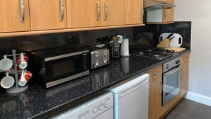 Uma cozinha com armários de madeira, bancada preta, micro-ondas, torradeira, fogão a gás e lava-louças.
