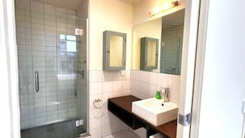 Uma casa de banho moderna com cabine de duche em vidro, lavatório branco e duas espelhas.