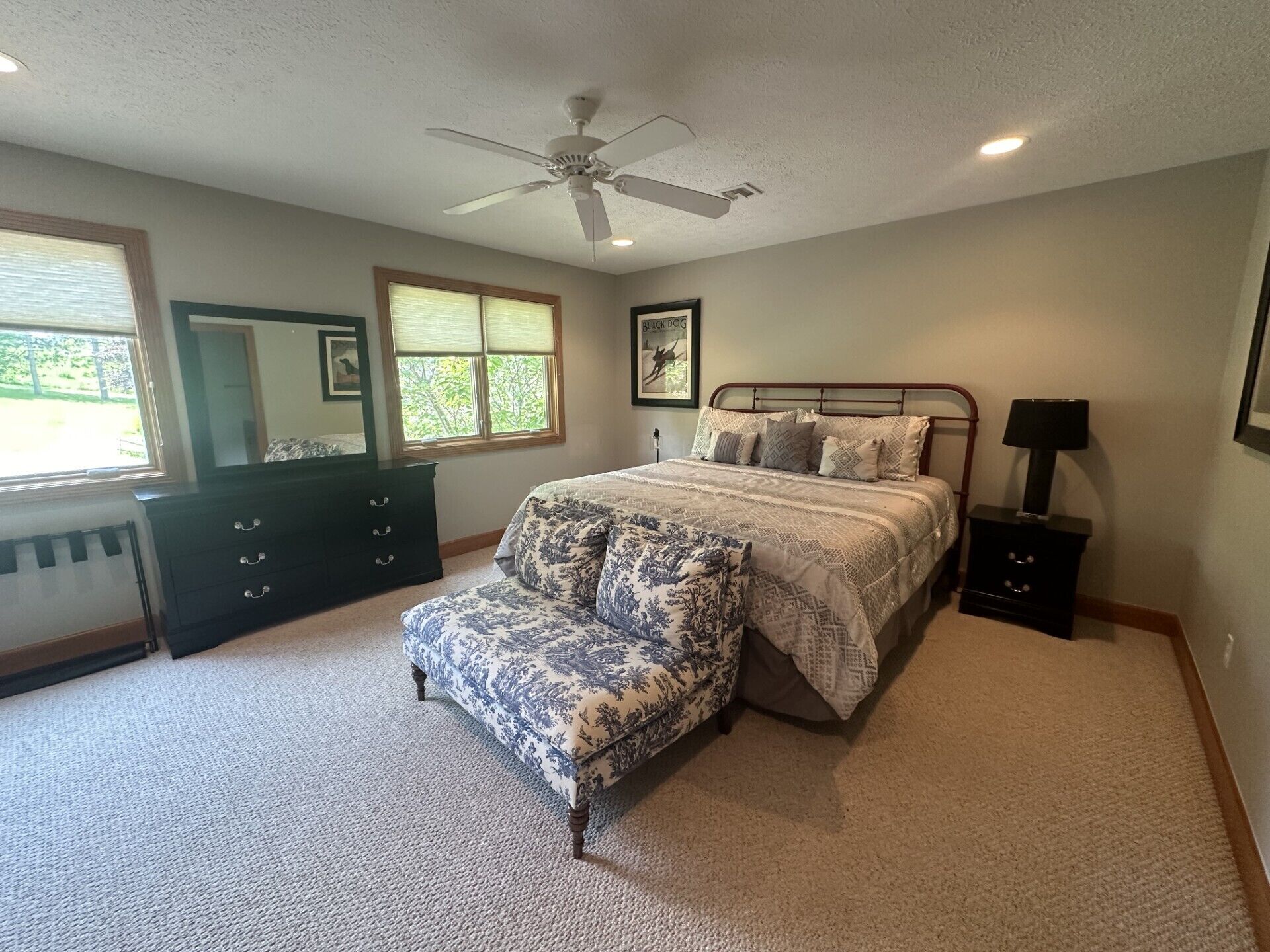 Quarto com cama, mesa de cabeceira, cômoda, cadeira, ventilador de teto e janela com persianas.