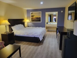 Quarto de hotel com cama, abajures, um quadro, um espelho, televisão e uma escrivaninha.