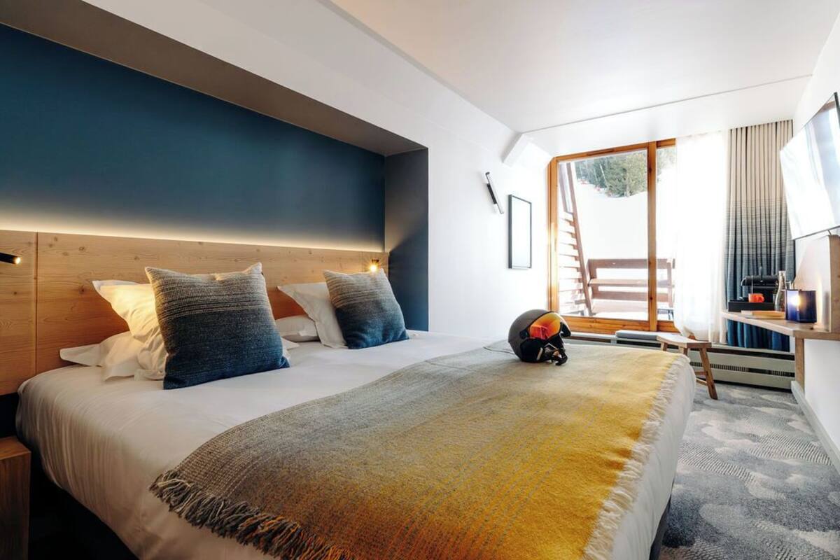 Quarto de hotel moderno com uma cama grande, cabeceira de madeira, televisão e varanda com vista.