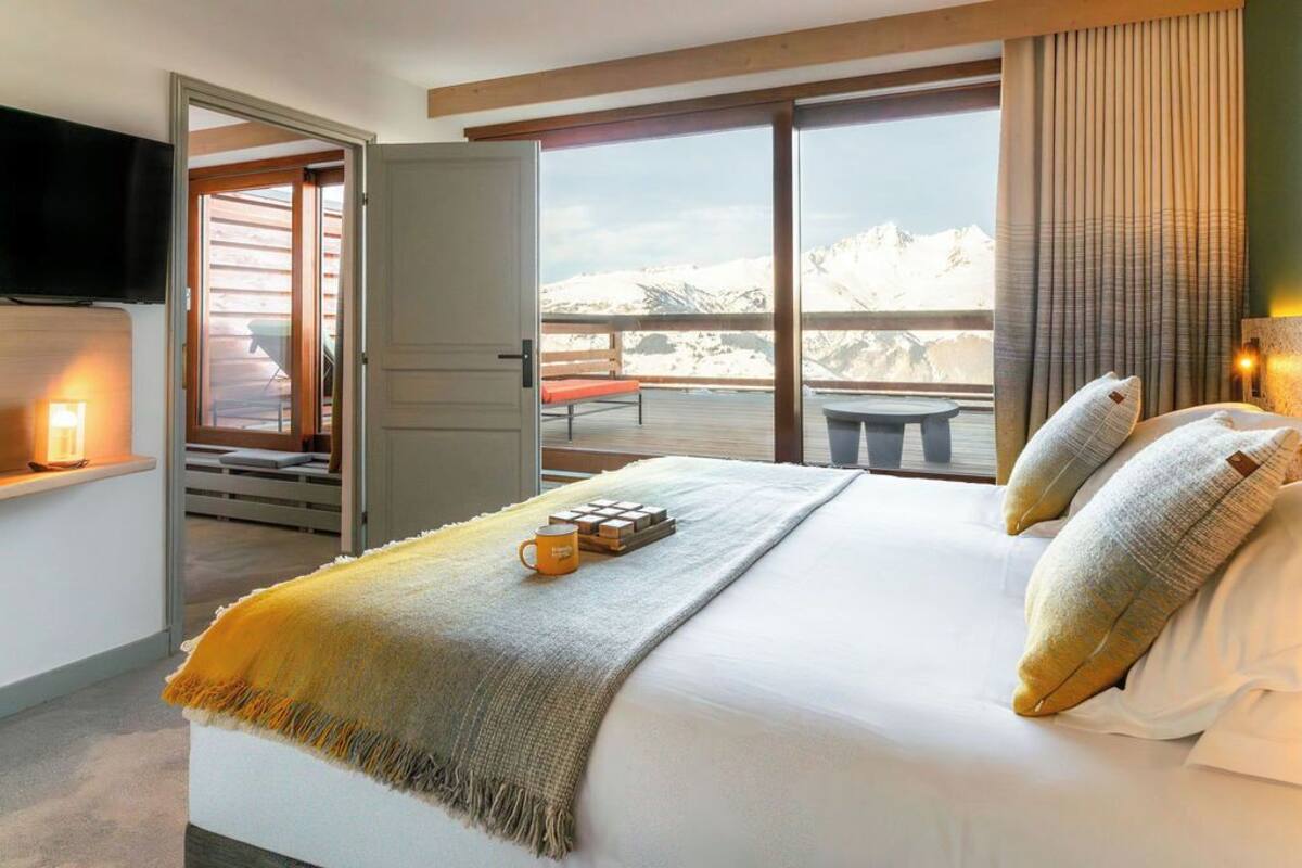 Quarto com uma cama, mesa de cabeceira, televisão e vista para uma montanha coberta de neve.