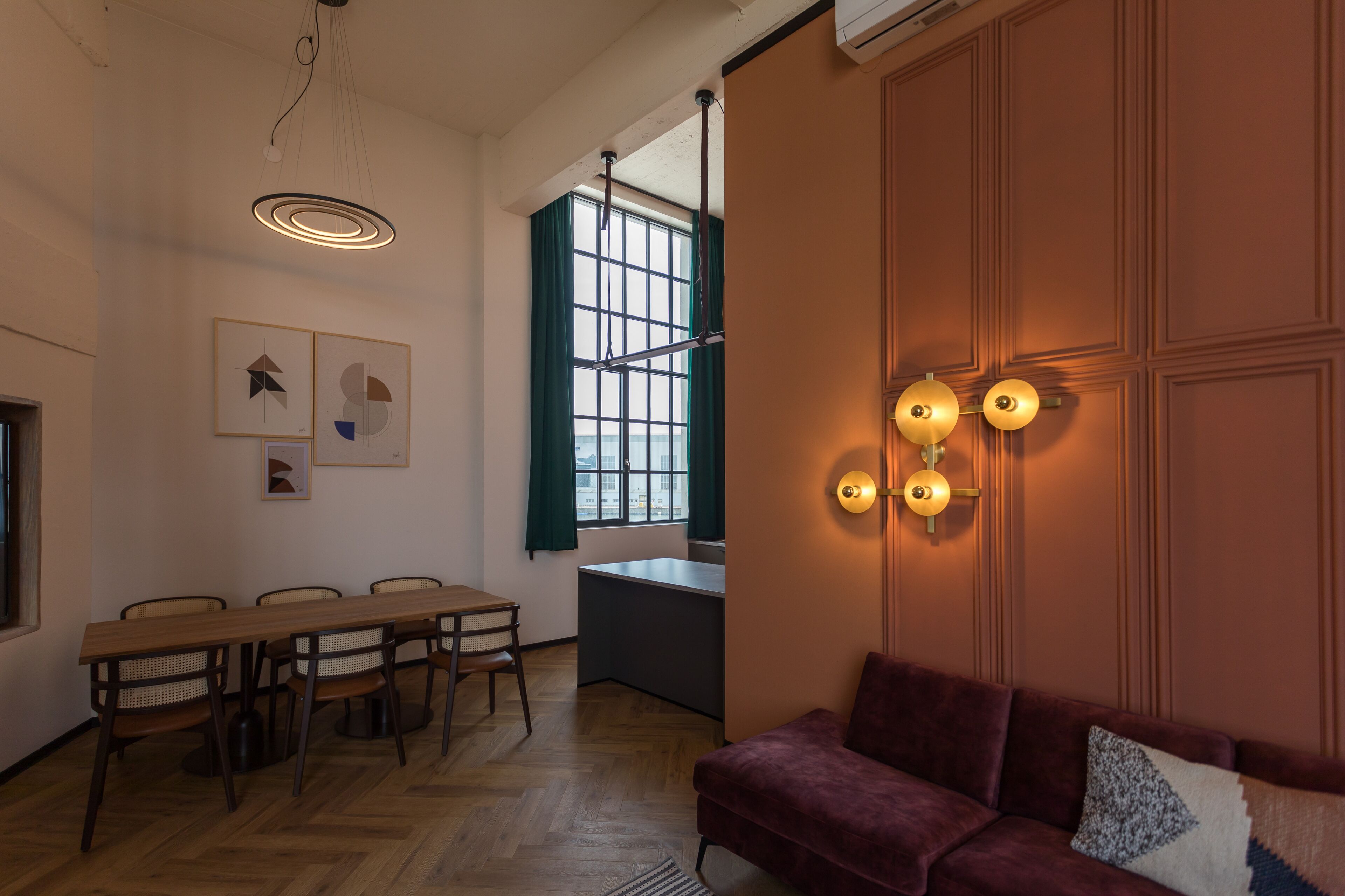 Uma sala de estar moderna com uma mesa de jantar de madeira, cadeiras estofadas, um sofá vermelho e iluminação embutida na parede.