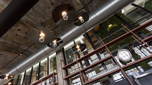 Um interior moderno com dutos aparentes, janelas amplas e diversos luminários.