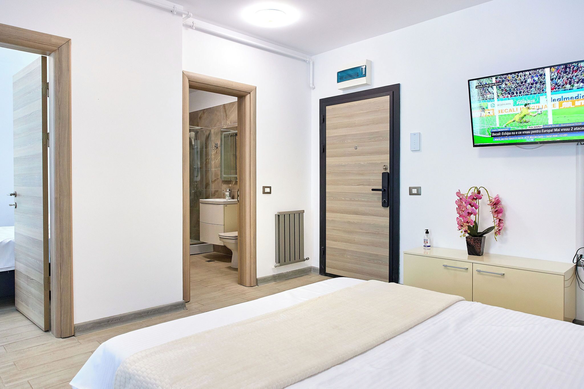 Quarto de hotel com cama, televisão, radiador e banheiro visível por uma porta aberta.