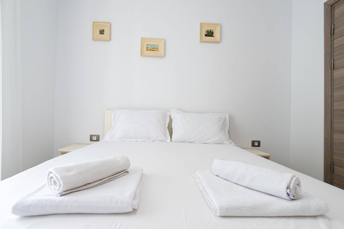 Quarto de hotel com uma cama grande, duas mesas de cabeceira e três quadros na parede.