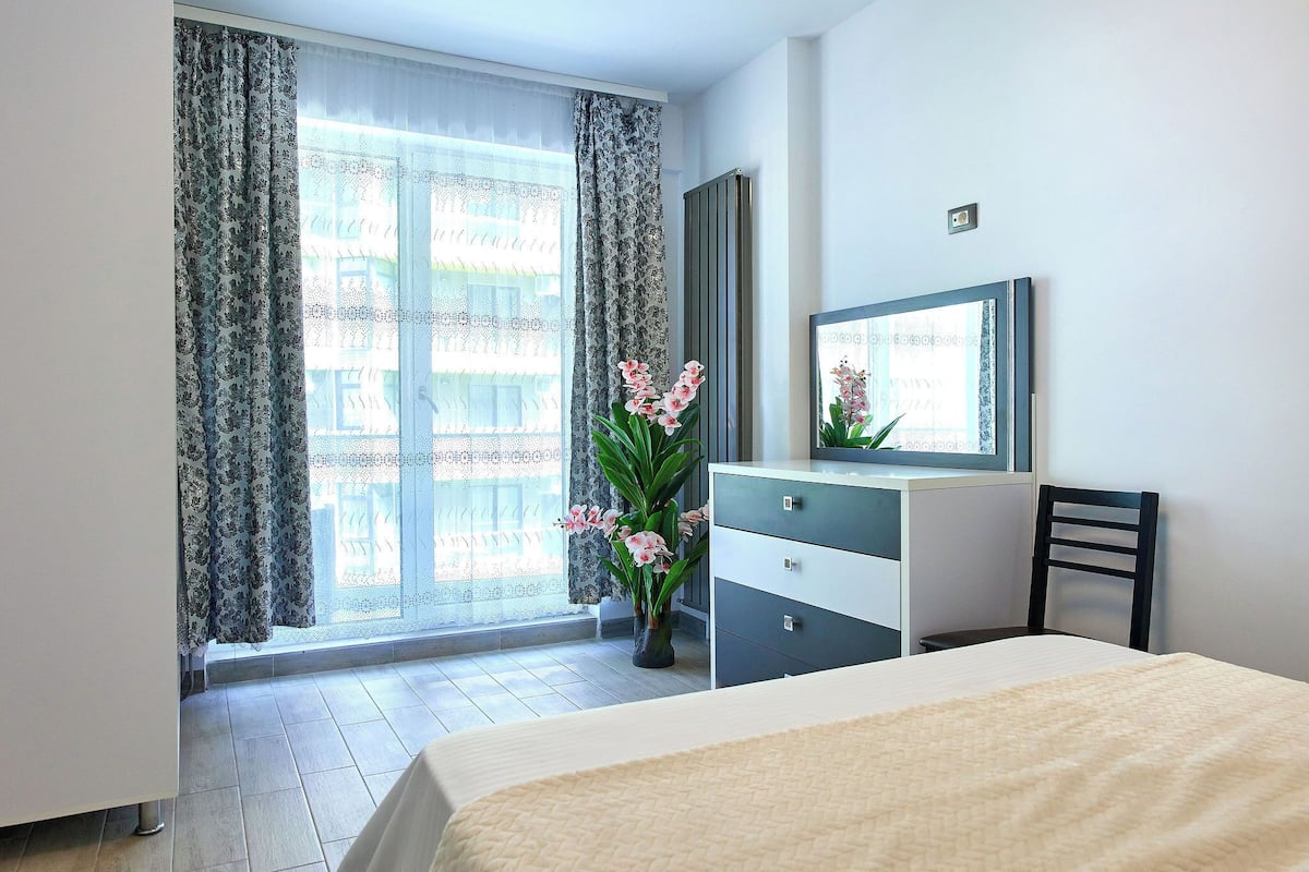 Quarto de hotel com cama, penteadeira, espelho e janela com cortinas.