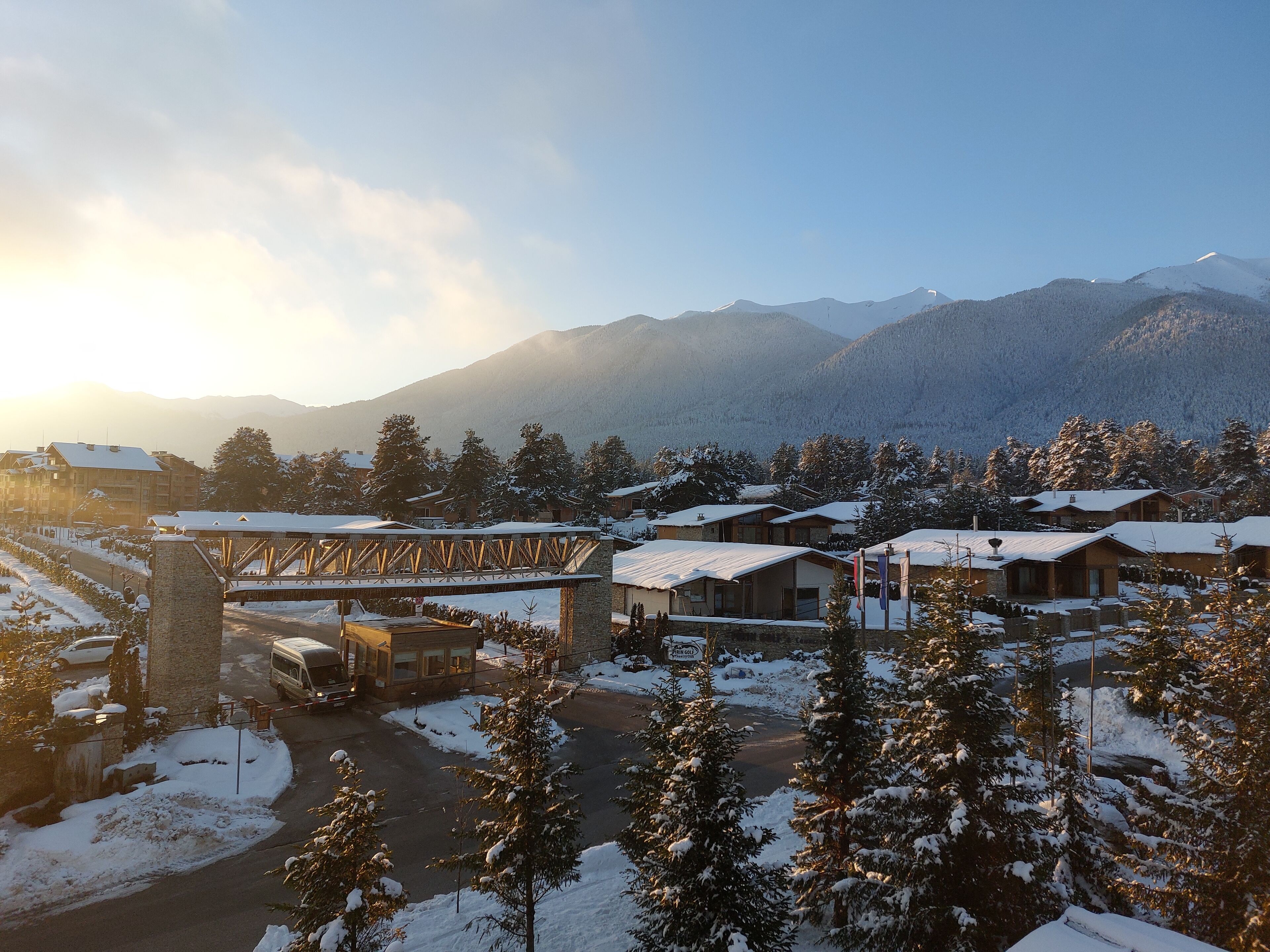 Estância coberta de neve com vários edifícios, uma ponte e montanhas ao fundo.