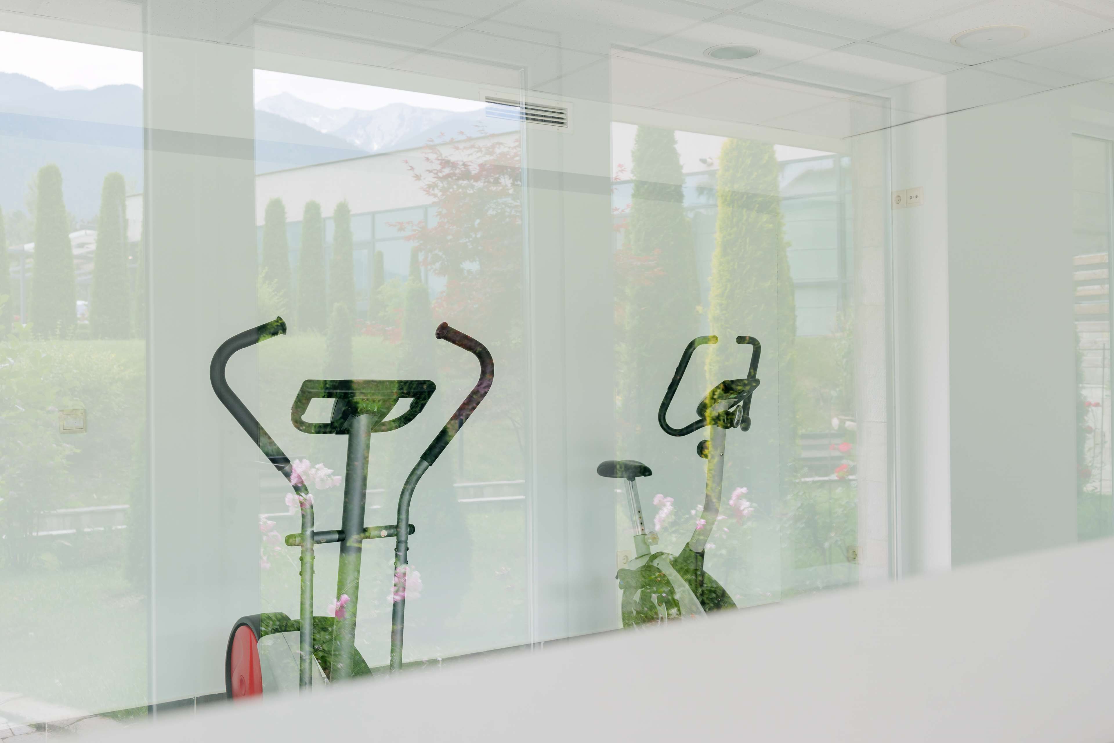 Quarto com amplas janelas, bicicletas ergométricas e vista para vegetação e montanhas.
