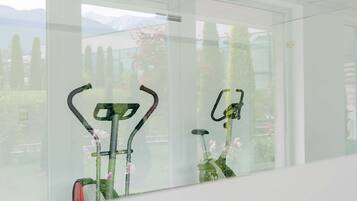 Quarto com amplas janelas, bicicletas ergométricas e vista para vegetação e montanhas.