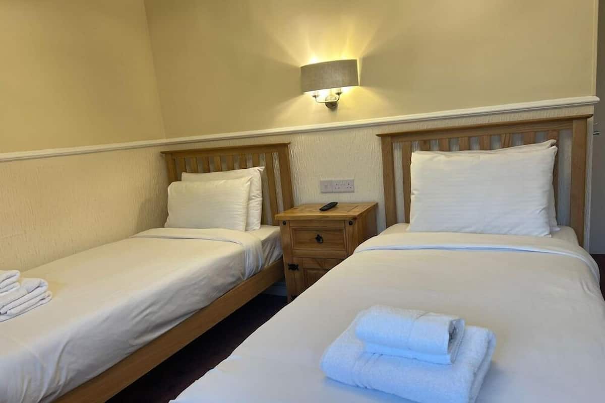 Quarto duplo com duas camas, mesa de cabeceira com abajur e luminária na parede.