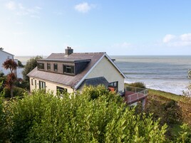 Uma casa à beira-mar com varanda e vista para o mar, rodeada por vegetação.