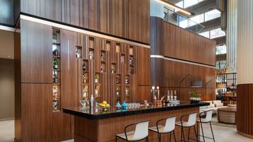 Uma área de bar moderna com painéis de madeira, bancada preta e banquetas.