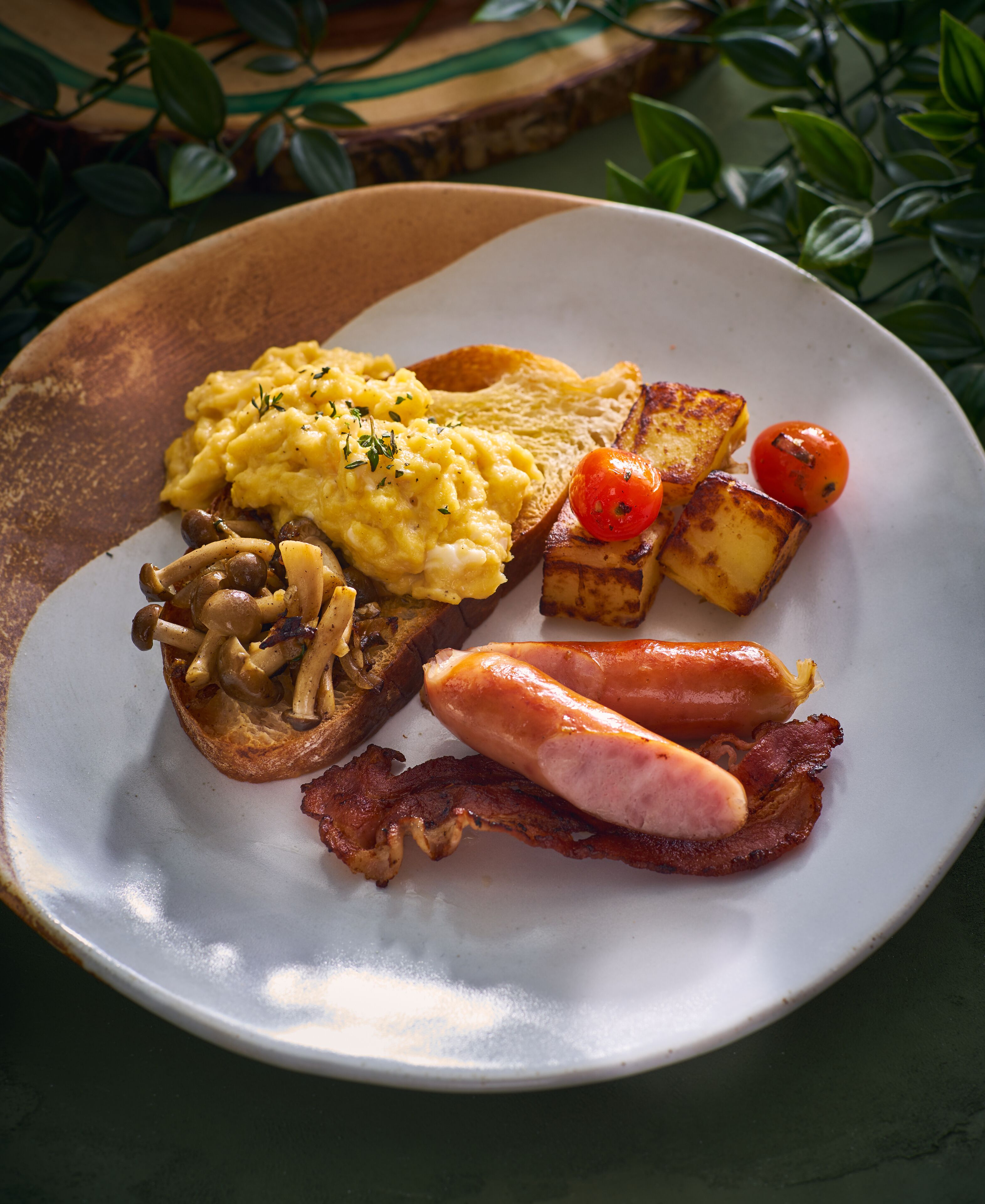 Prato de comida de café da manhã com ovos mexidos, torradas, linguiças, bacon, cogumelos, batatas assadas e tomates cereja.