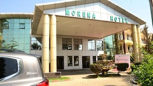 Um hotel chamado "Morena Hotel", com fachada moderna, janelas amplas e área de entrada ajardinada.