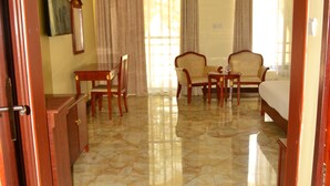 Quarto de hotel com uma cama, dois poltronas, uma mesinha e uma escrivaninha com cadeira.