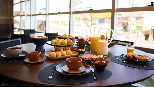 Mesa de café da manhã com diversos alimentos, uma xícara de café e um jarro de suco.