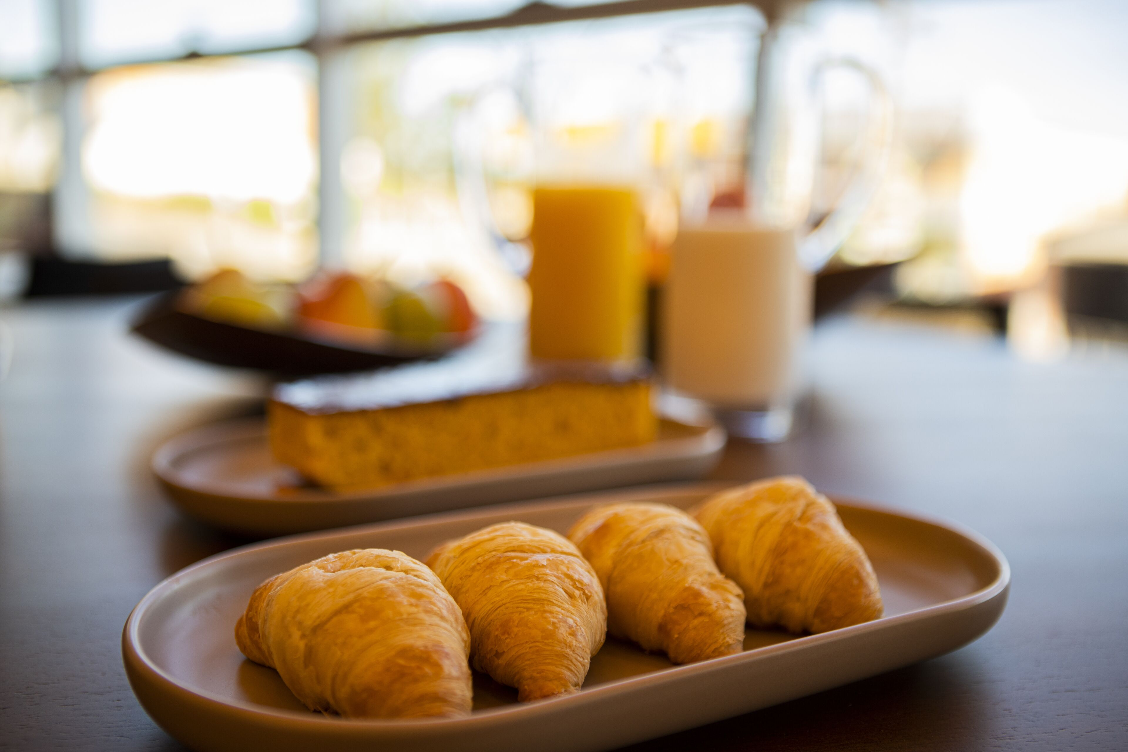 Croissants num prato, um copo de sumo de laranja e uma taça de fruta sobre uma mesa.