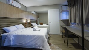 Quarto de hotel com duas camas, uma escrivaninha, uma cadeira, uma televisão e aparelho de ar condicionado.