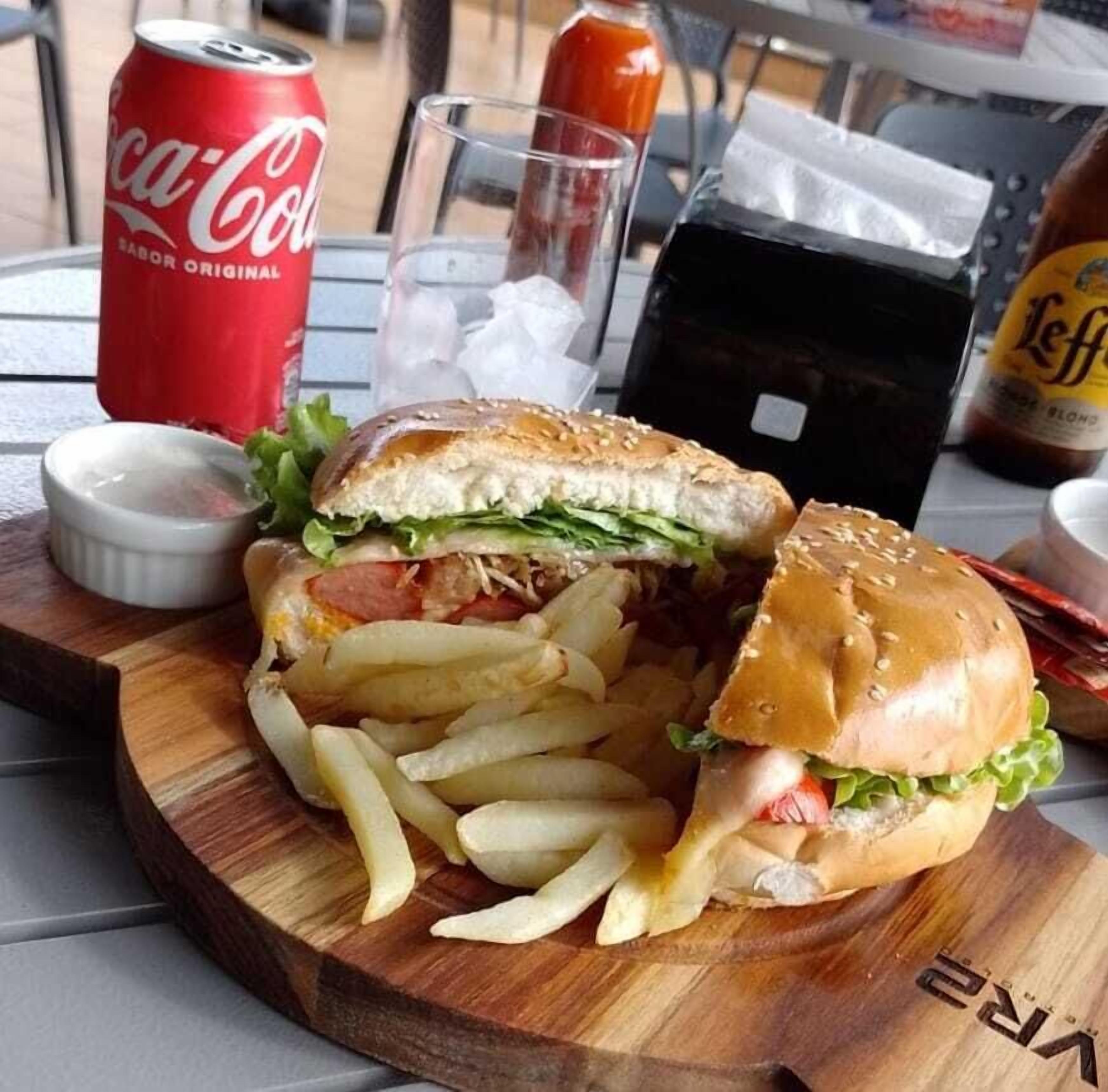 Uma refeição com sanduíche, batatas fritas e bebida, servida em uma tábua de madeira.