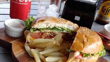 Uma refeição com sanduíche, batatas fritas e bebida, servida em uma tábua de madeira.