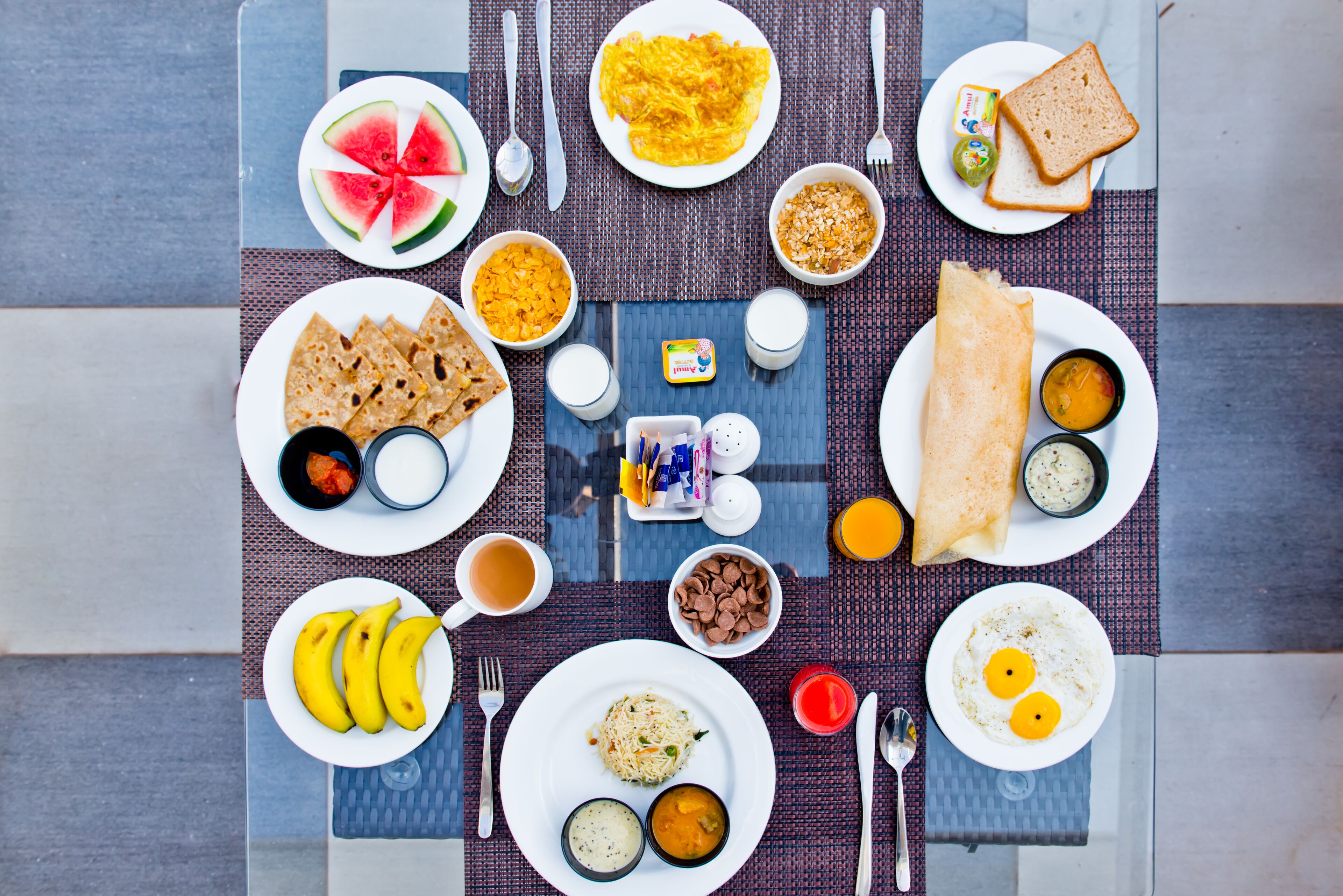 Mesa posta com diversos pratos de café da manhã, incluindo torradas, ovos e frutas.