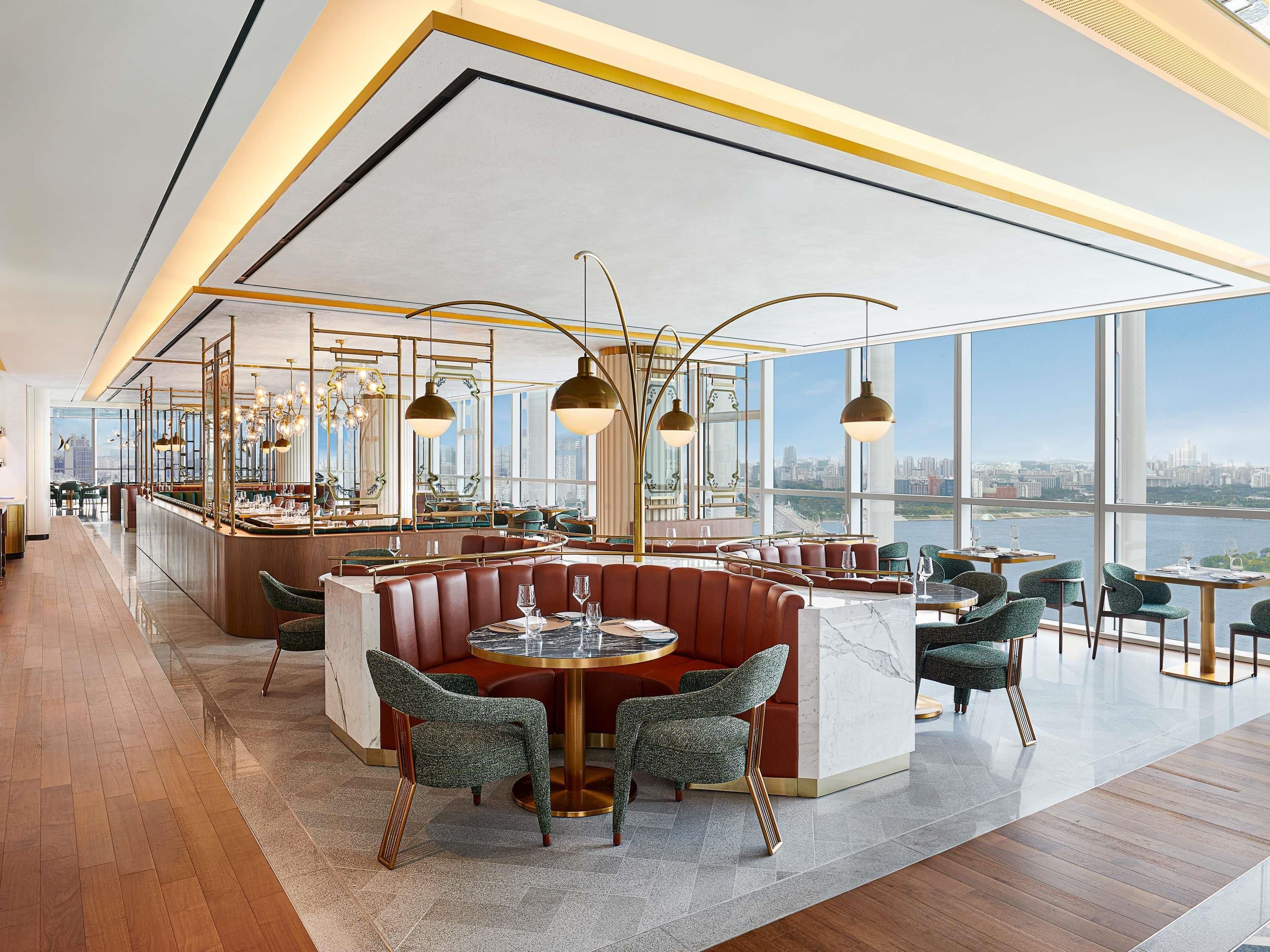 Um restaurante moderno com teto alto, amplas janelas e vista para a cidade.