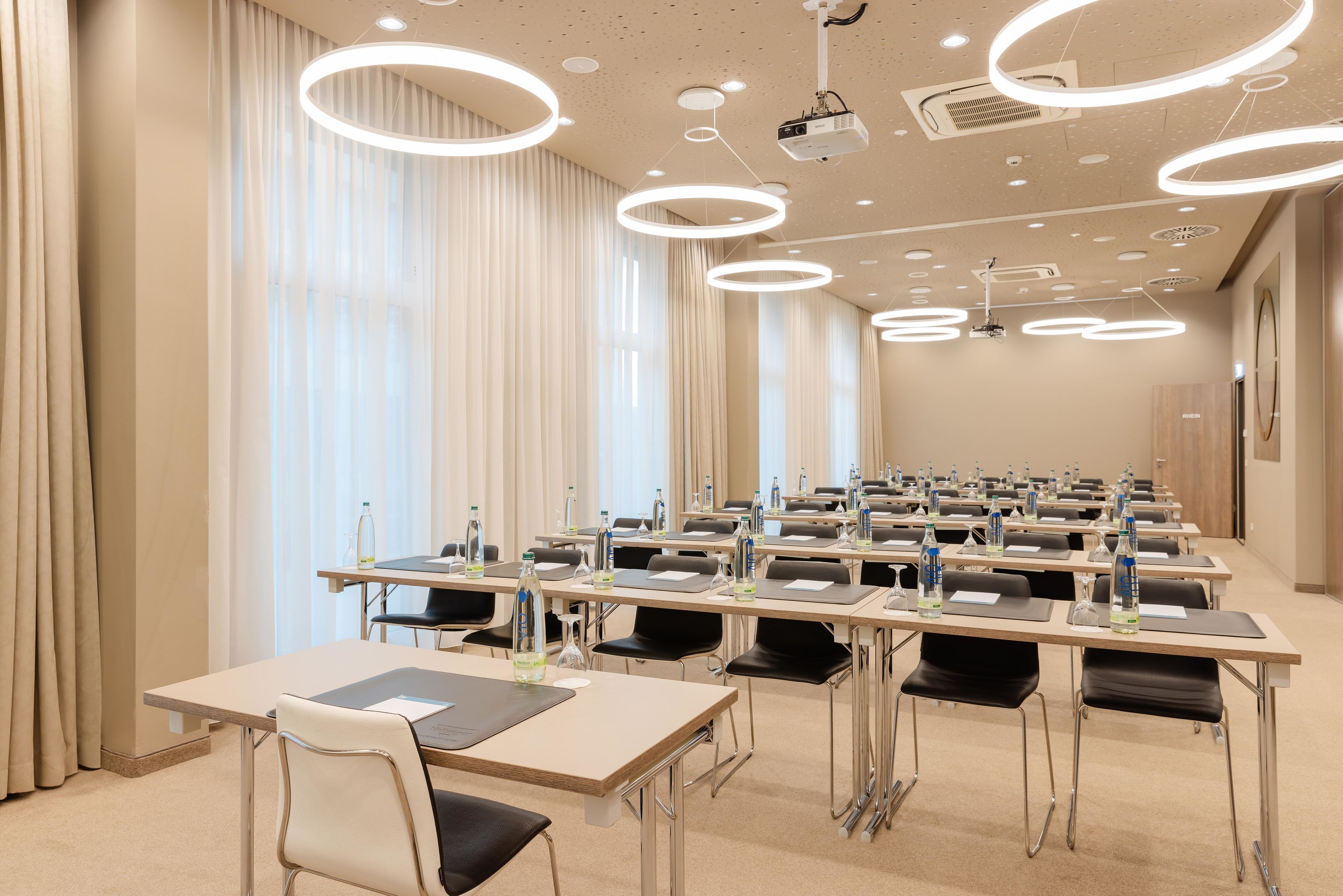 Uma sala de conferência com várias mesas, cadeiras e um projetor.