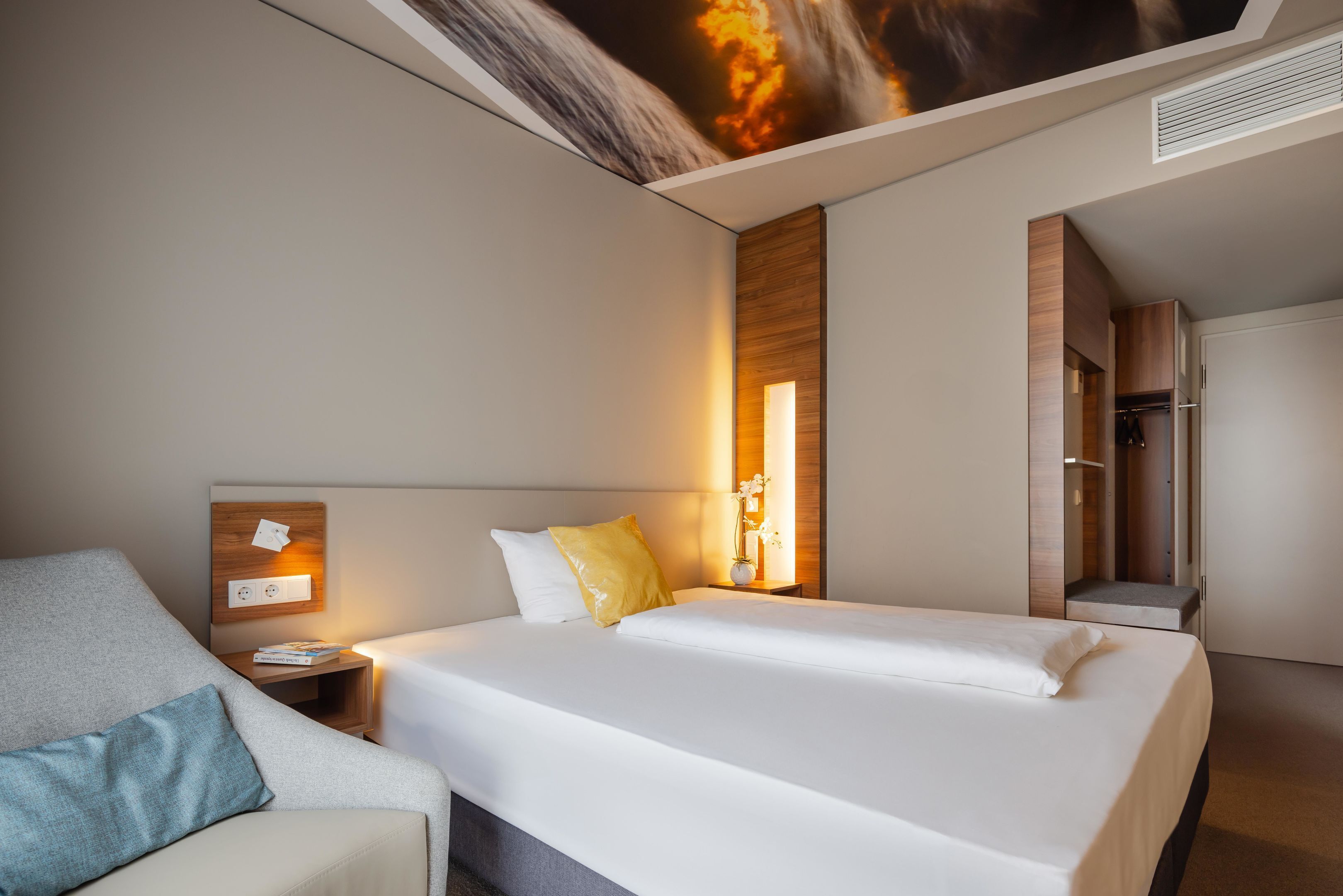 Quarto de hotel com uma cama, mesa de cabeceira, abajur, espelho e guarda-roupa.