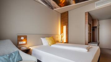 Quarto de hotel com uma cama, mesa de cabeceira, abajur, espelho e guarda-roupa.
