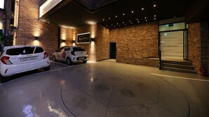 Entrada de hotel com fachada de tijolos, uma placa e dois carros estacionados.