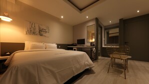 Quarto de hotel moderno com uma cama grande, uma mesa, uma cadeira e um espelho.