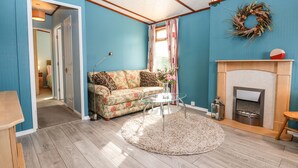 Uma sala de estar com um sofá floral, uma mesa de centro de vidro, uma lareira e uma parede azul.