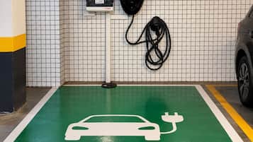 Vaga de estacionamento com piso verde demarcada para veículos elétricos, uma estação de carregamento e um carro estacionado à direita.