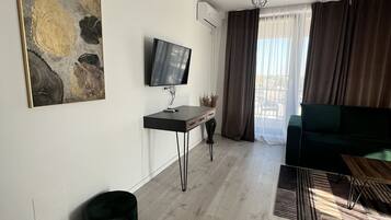 Uma sala de estar moderna com uma TV de tela plana, um sofá preto e um grande quadro abstrato na parede.