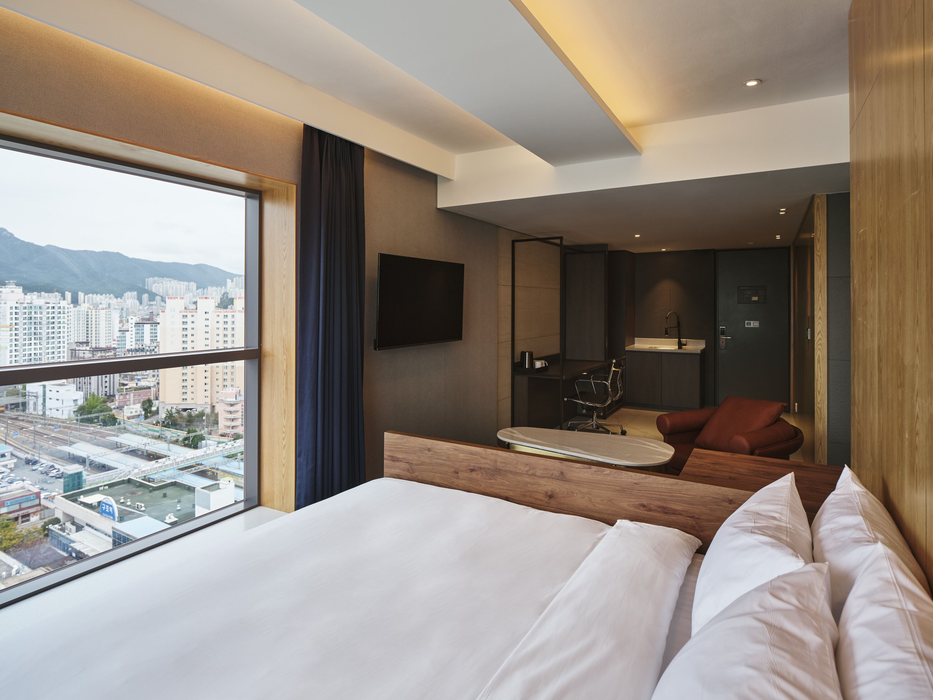 Quarto de hotel moderno com uma cama grande, escrivaninha, cadeira, espelho e vista para a cidade.