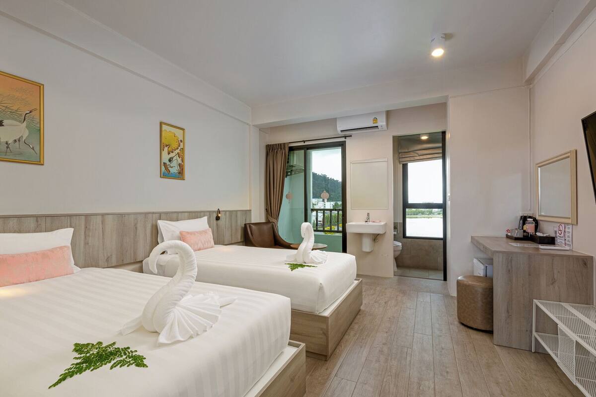 Quarto de hotel com duas camas, uma escrivaninha, uma pia e vista para o exterior.