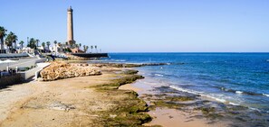 Uma área costeira com um farol, falésias rochosas e um calçadão pavimentado ao longo da praia.