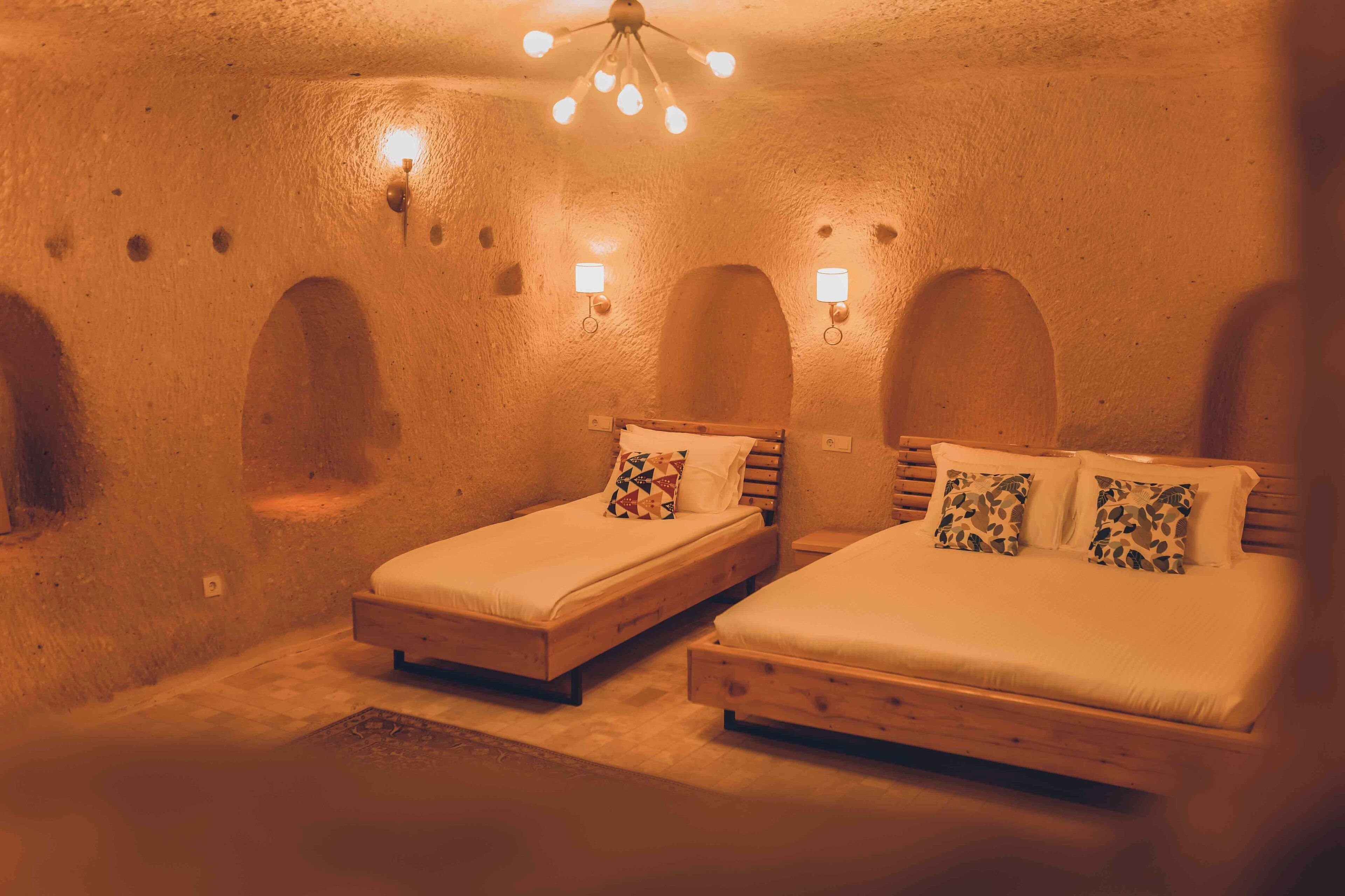 Um quarto aconchegante, tipo caverna, com duas camas de madeira, cada uma com um travesseiro e uma luminária fixada na parede.