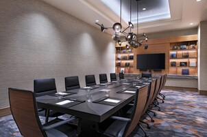 Uma sala de conferências com uma mesa comprida, cadeiras pretas e um lustre moderno.