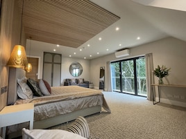 Quarto moderno com uma cama grande, um sofá, um espelho e vista para o exterior através de uma porta de correr de vidro.