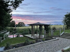 Um gazebo com vista para um pôr do sol sobre um campo.