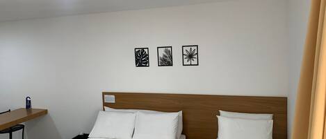Quarto de hotel com duas camas, uma escrivaninha e três obras de arte nas paredes.