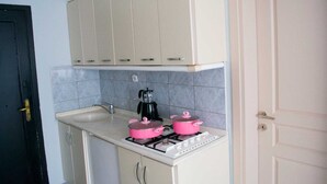 Cozinha compacta com fogão a gás, cafeteira e panelas cor-de-rosa na bancada.
