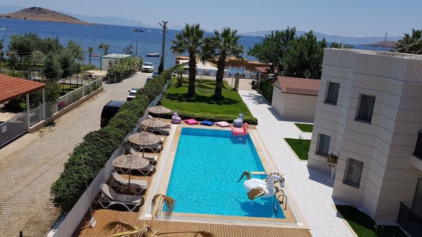Piscina com espreguiçadeiras e guarda-sóis, rodeada por vegetação e vista para o mar.