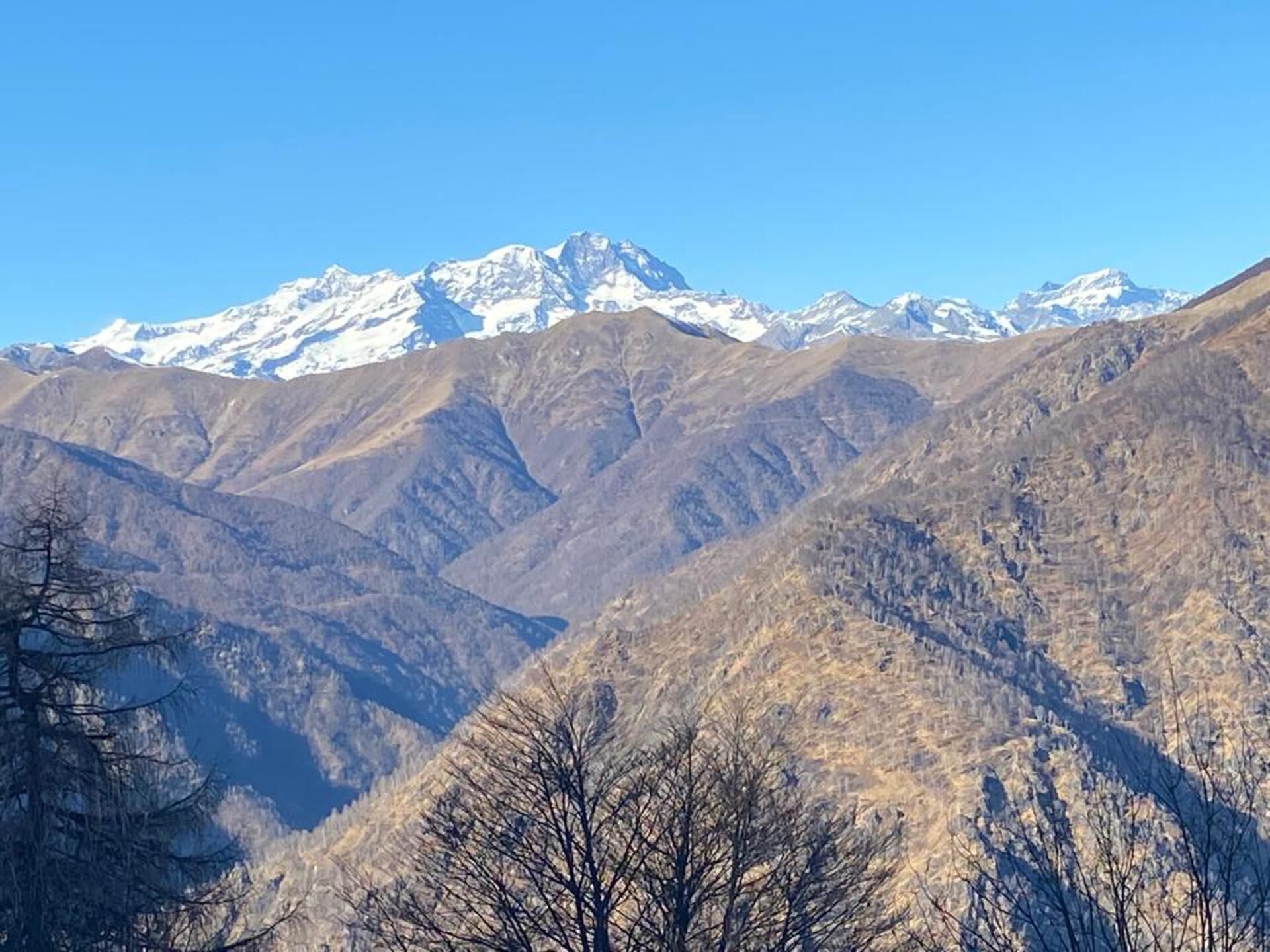 Paisagem montanhosa com picos nevados e colinas áridas.
